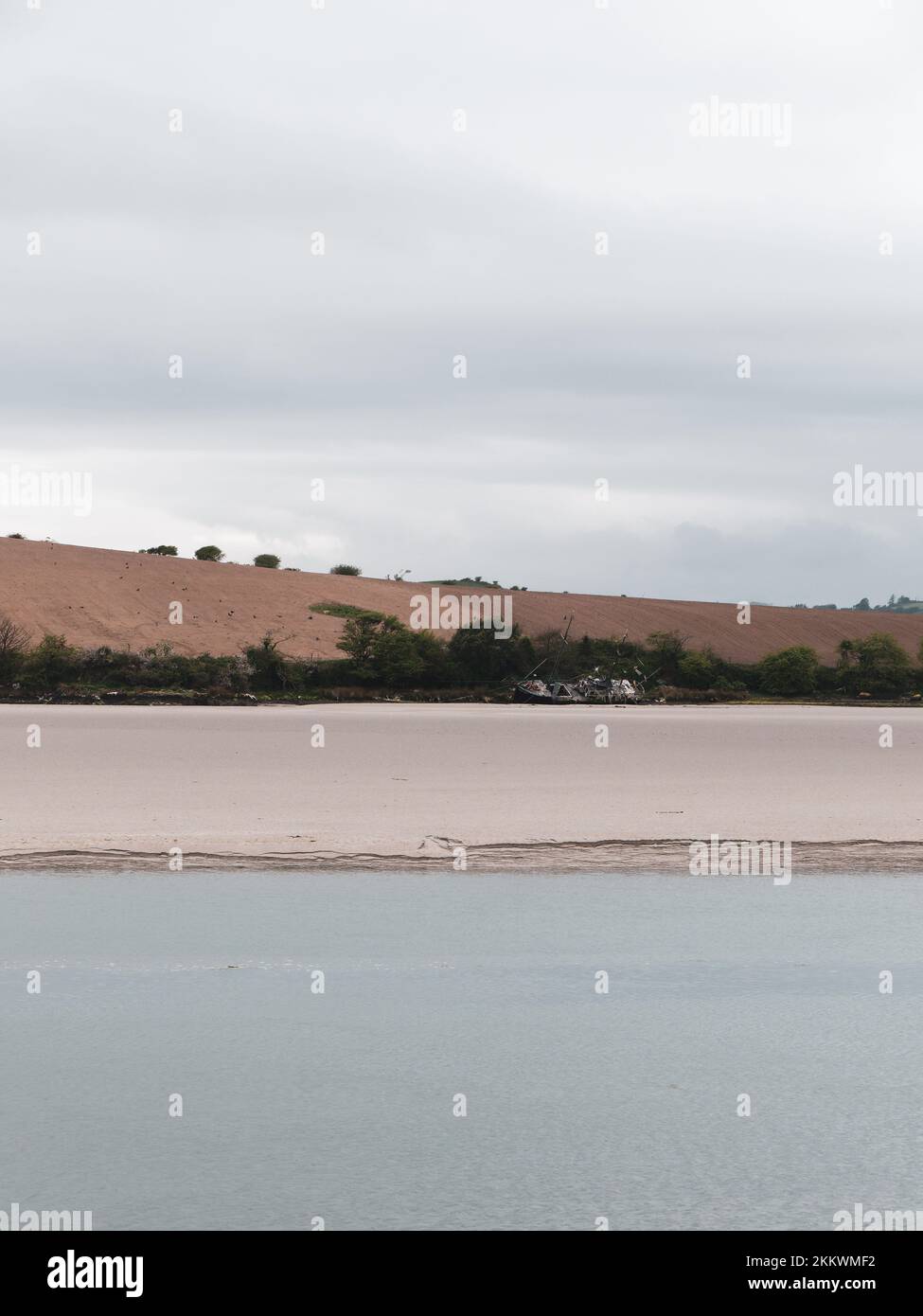 Sandy seashore. Calm water. The remains of an old ship on the shore. A ...