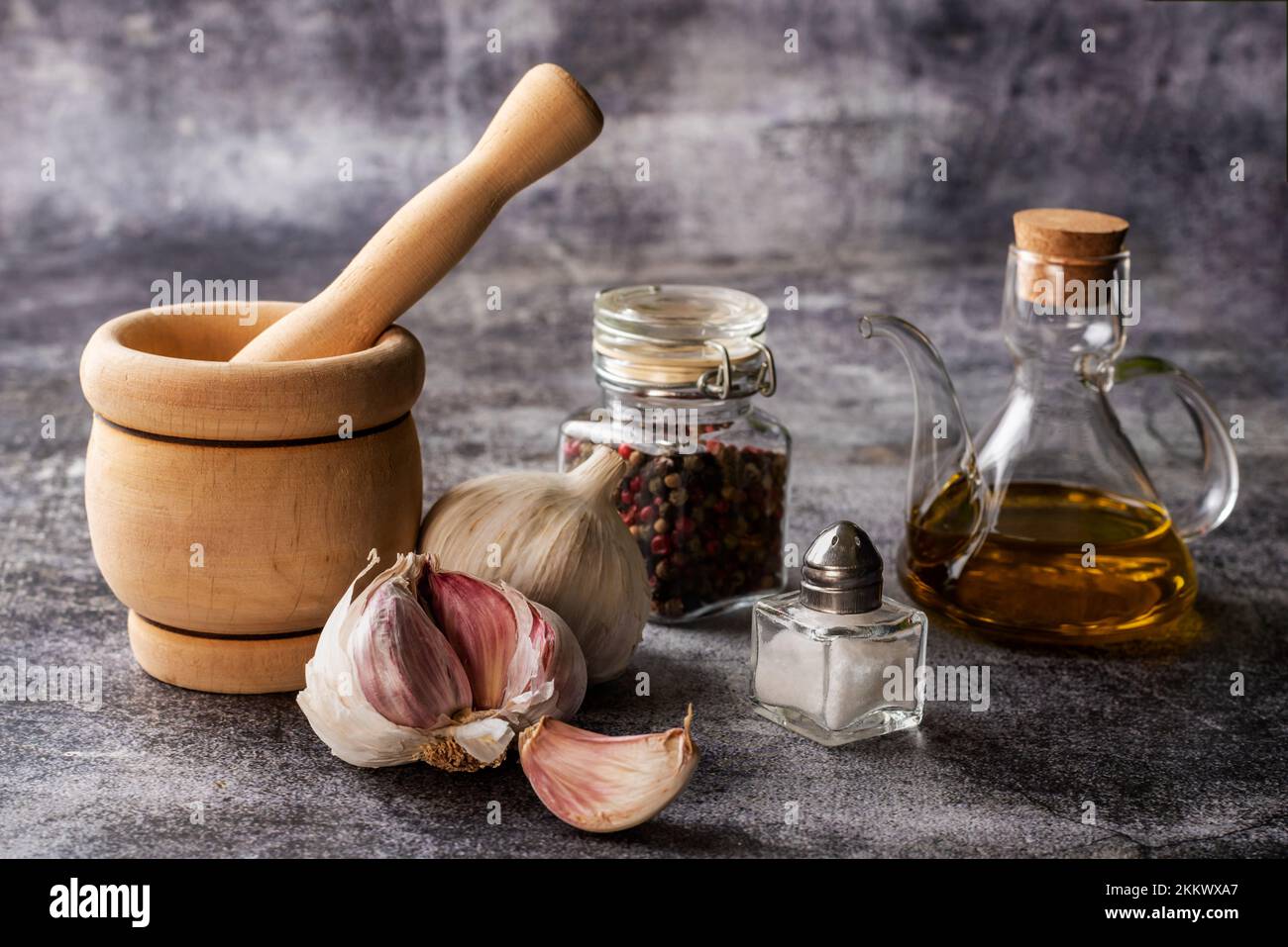 Oil can, peppercorn jar, wooden mortar, salt and garlic on a gray stone ...