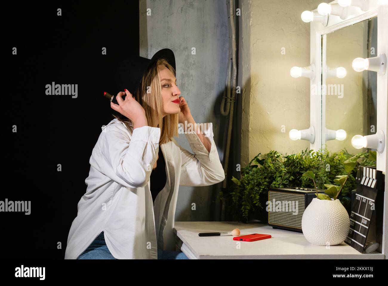 Stylish young beauty at dressing room mirror applies red lipstick on ...