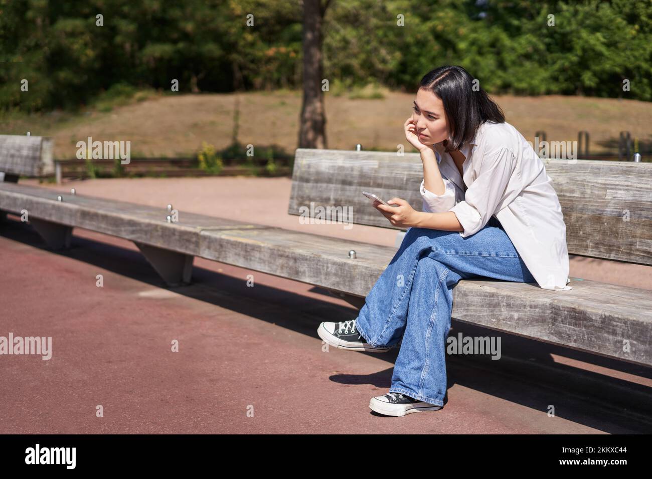 Portrait of asian girl sitting with smartphone feeling sad, looking ...