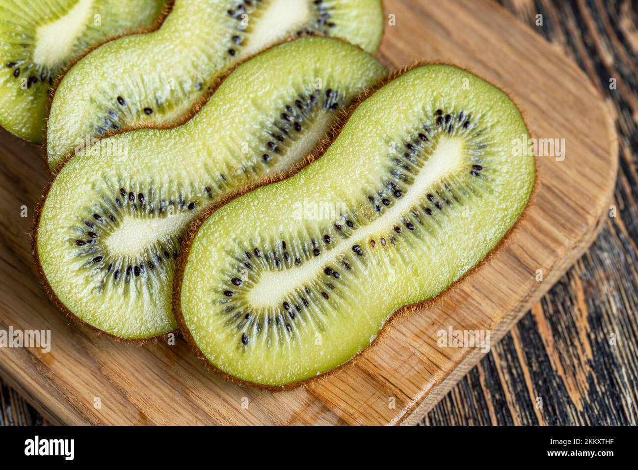 Kiwi slices cut with a knife on a board, cutting ripe green kiwi into ...