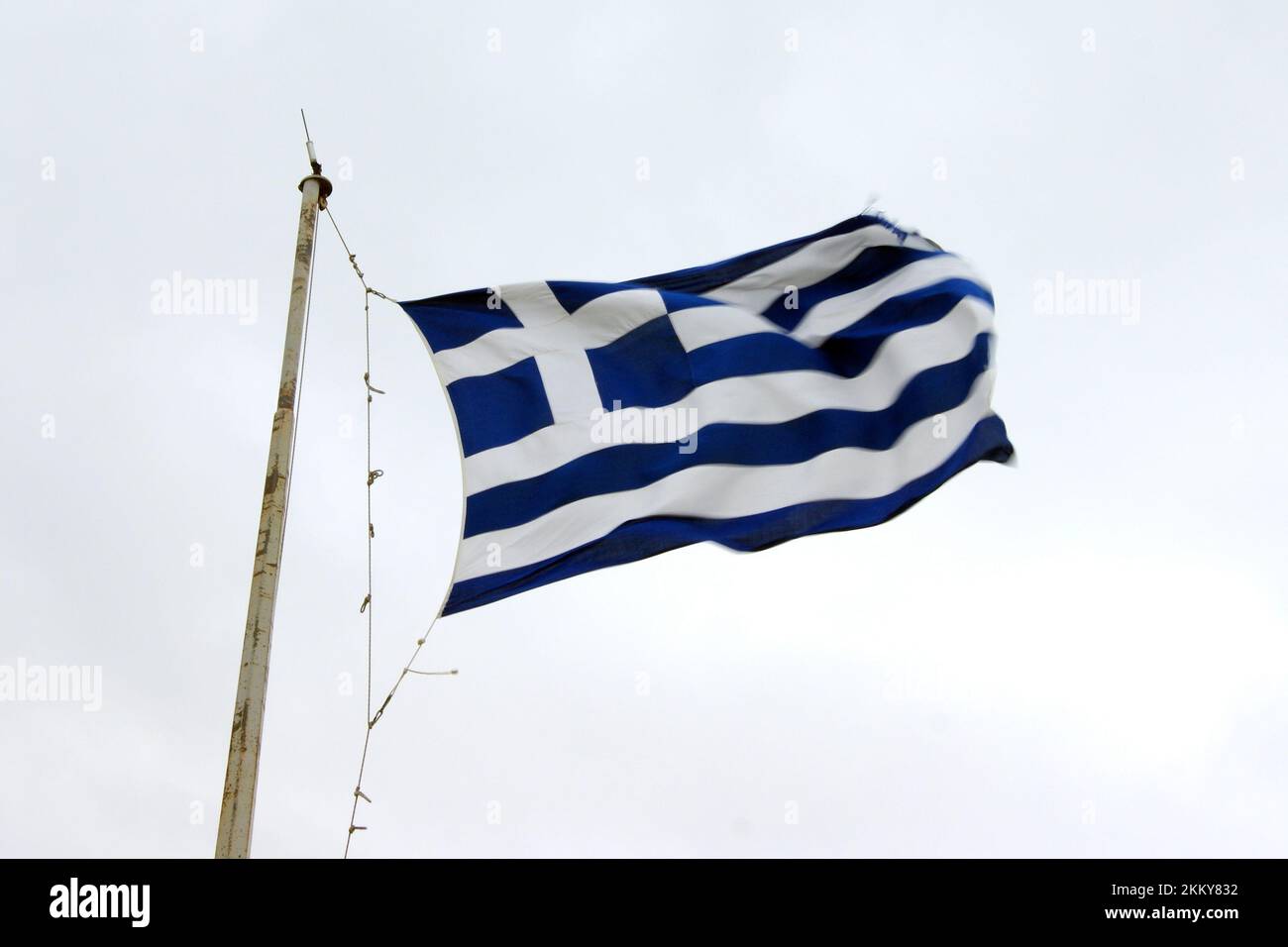 Flag of Greece flying on a staff on light blue cloudy sky background ...