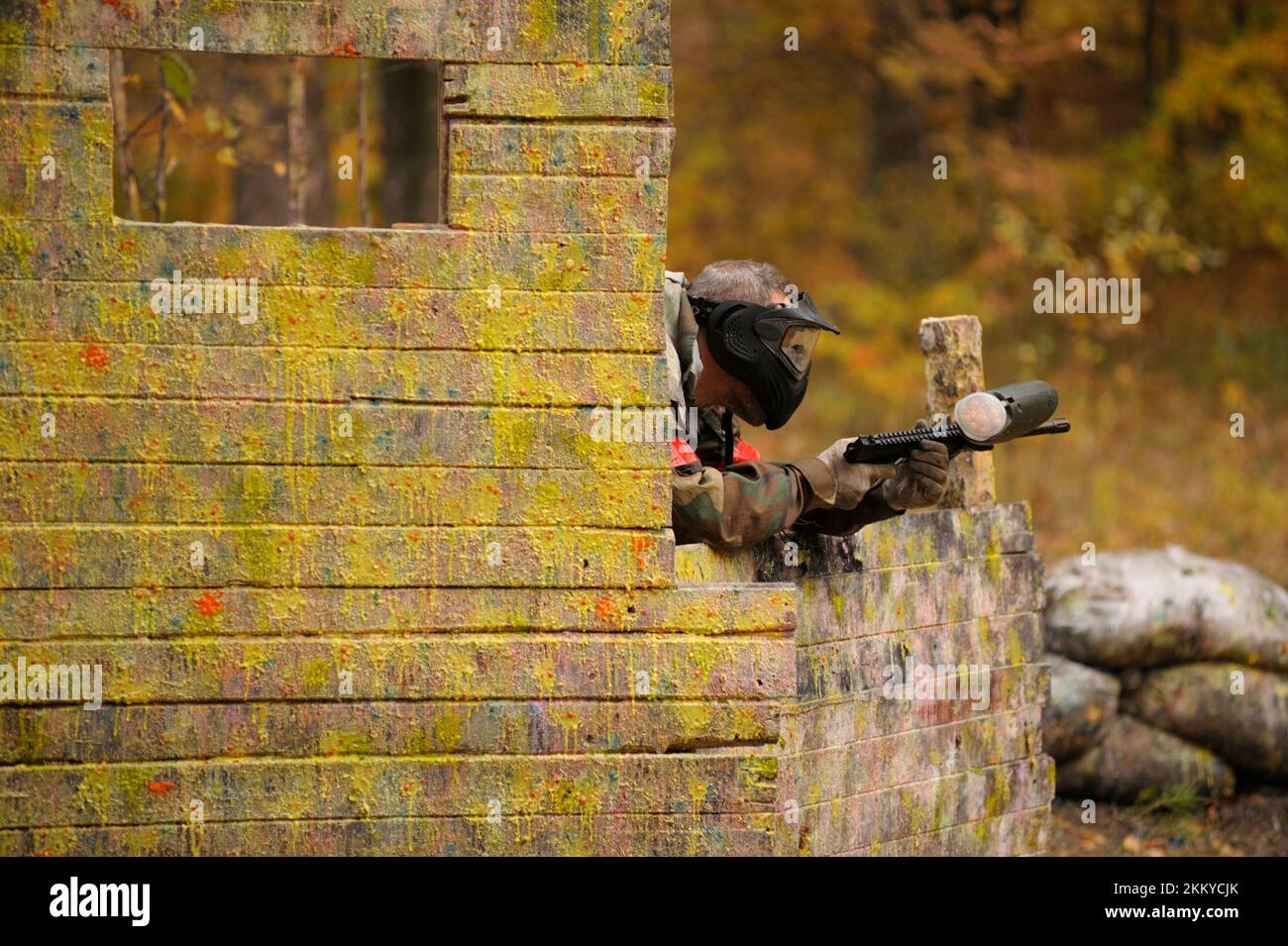 Man player shooting with a paintball gun hiding behind wooden shelter ...