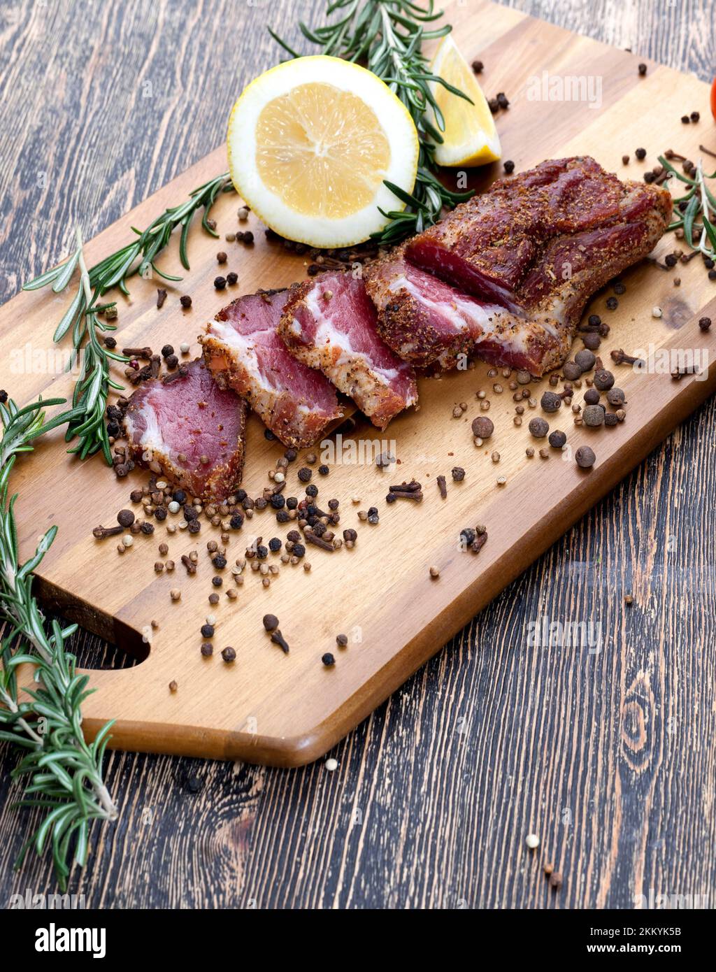 dried and spiced meat sliced on a wooden board, spices, pepper, lemon ...