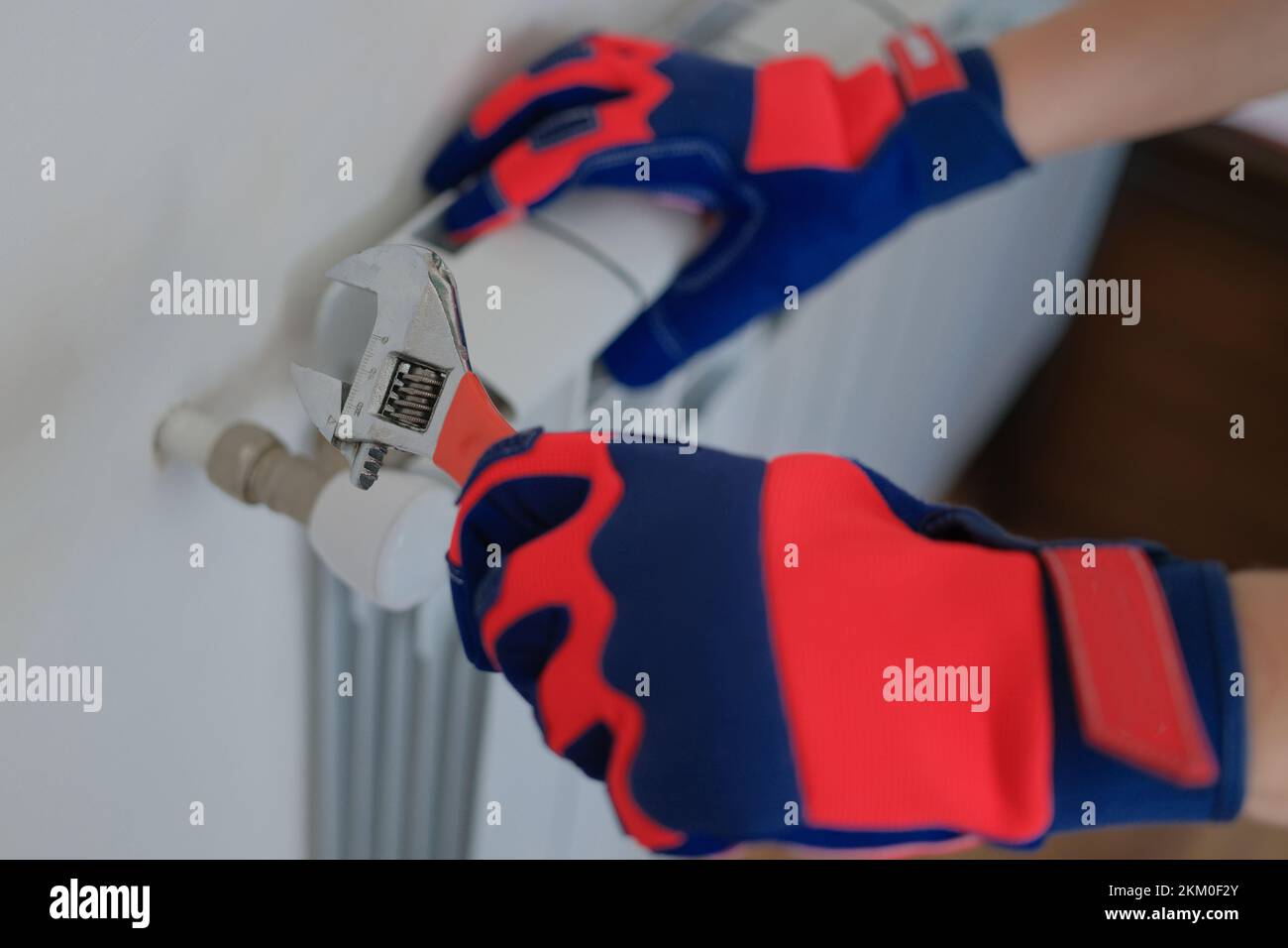 Man plumber hands in gloves installing heating radiator using wrench ... Man plumber hands in gloves installing heating radiator using wrench ...
