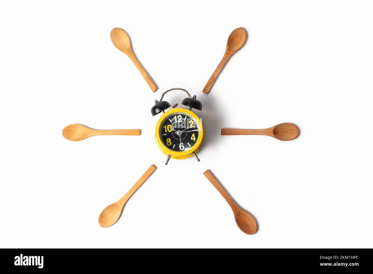 Top view of yellow alarm clock with wooden circle spoons around it ...