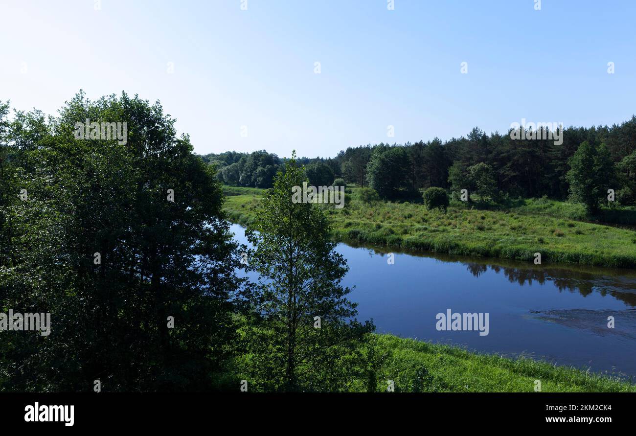 a summer landscape with green grass and deciduous trees and a river ...
