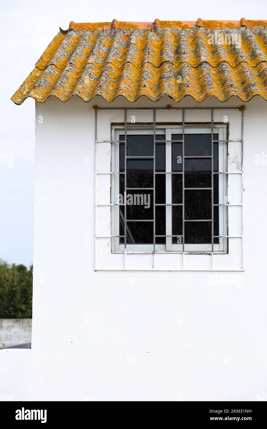 Whitewashed facade with window with forged metal grill and uralite roof ...