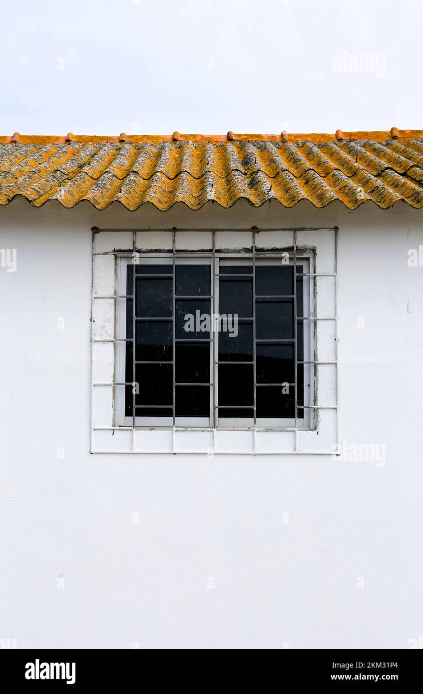 Whitewashed facade with window with forged metal grill and uralite roof ...
