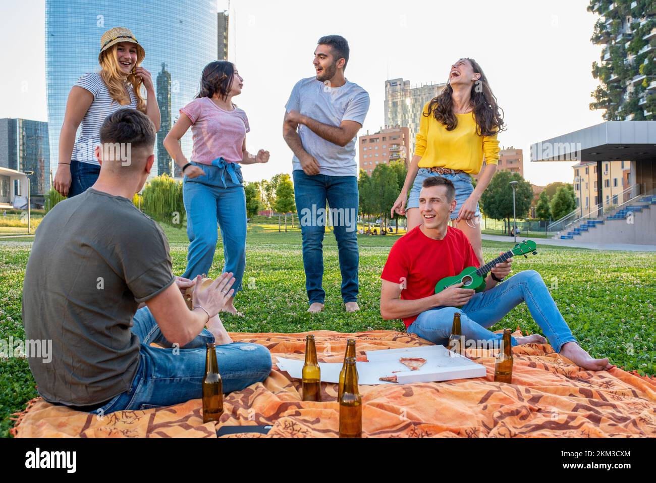 group of young couples having an urban picnic in a city park, guys ...