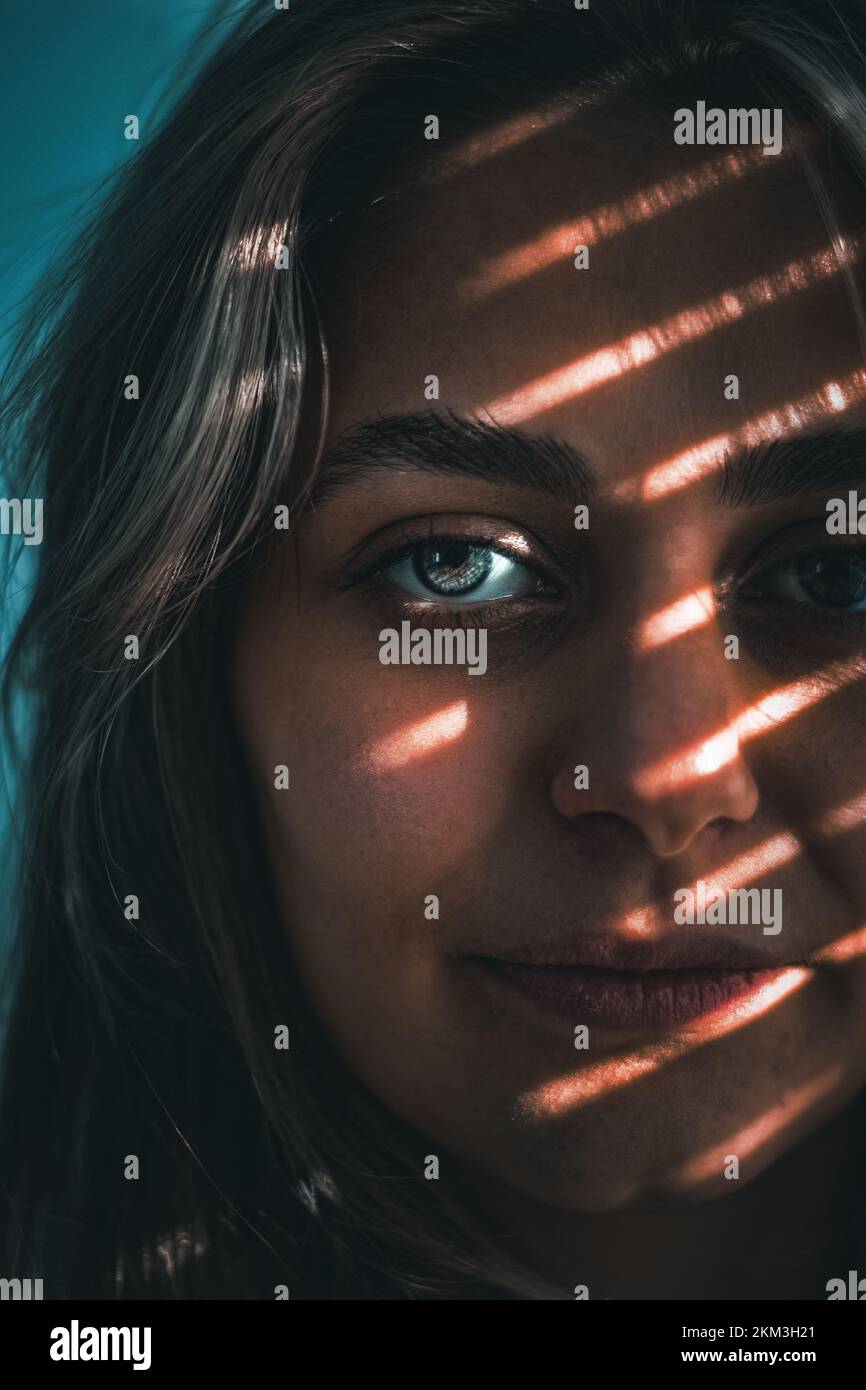 A portrait of a young Caucasian female with blue eyes under blinds ...