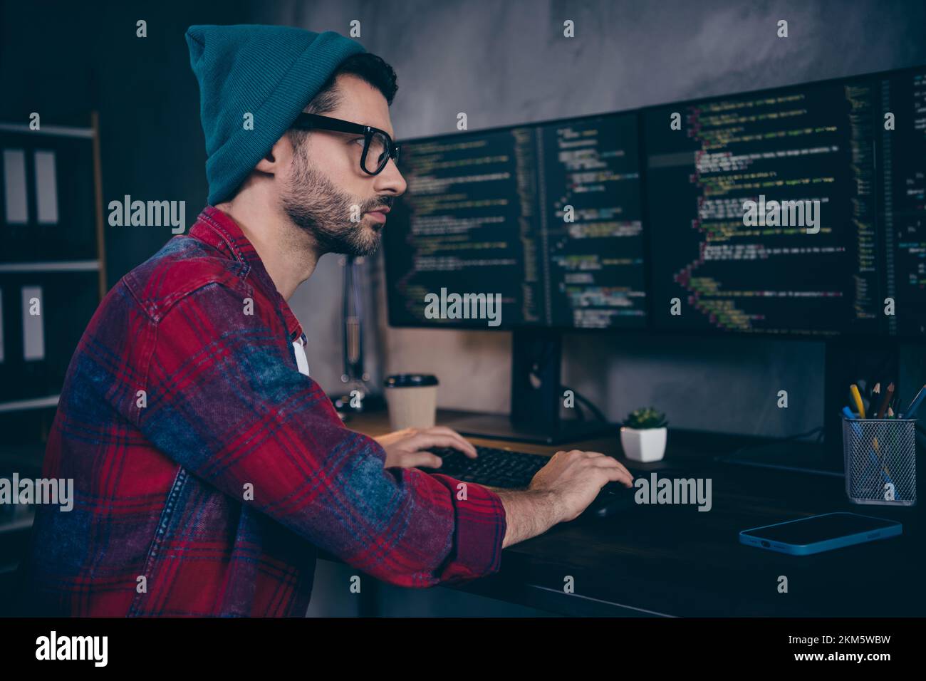 Photo of clever cool coder dressed hat glasses creating program modern gadget indoors workplace ...