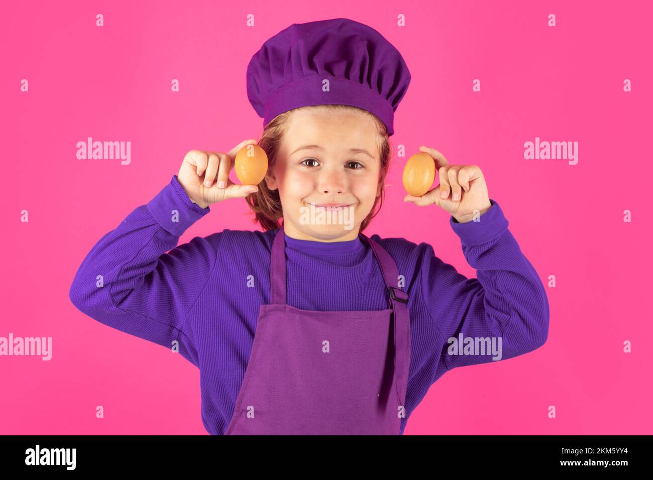 Child cook hold eggs. Child in cook uniform. Chef kid isolated on pink ...