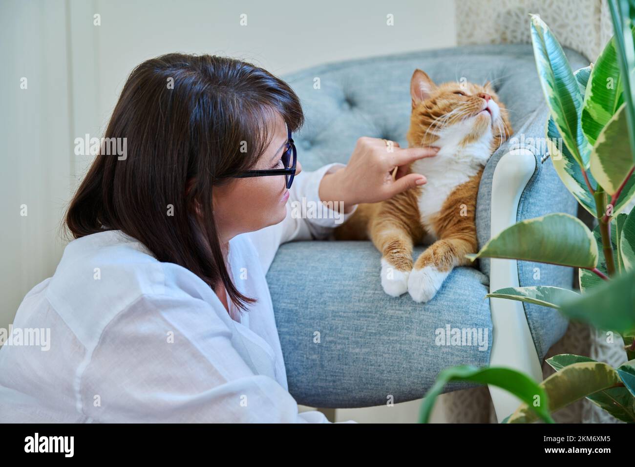 Middle aged woman touching ginger pet cat, home interior background ...
