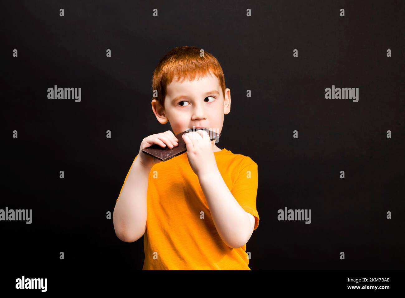 portrait the face of a small red-haired boy bites and bites a bar of ...
