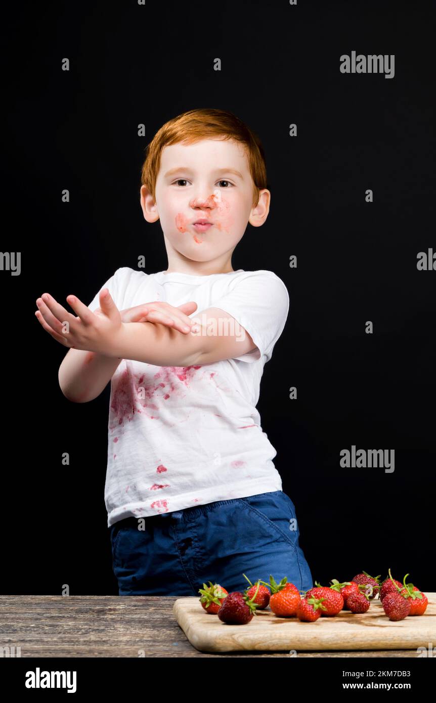 red-haired boy with ripe red strawberries, portrait of a child closeup ...