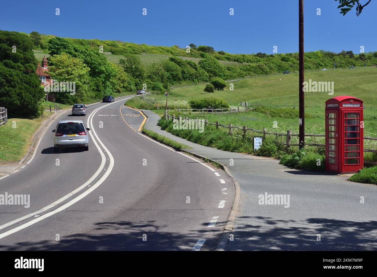 An iconic red telephone box beside a main road with double white lines ...