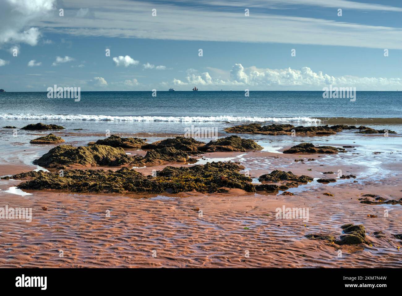Rocky outcrops and ripples in the sand at Goodrington beach, with boats ...
