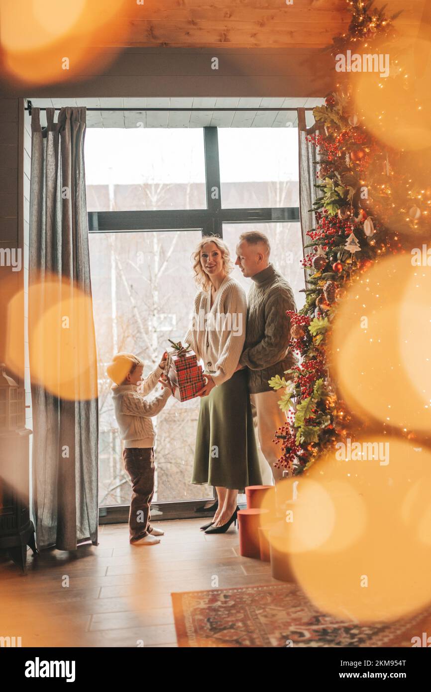 Portrait of happy family in knitted beige sweaters waiting Santa indoor ...