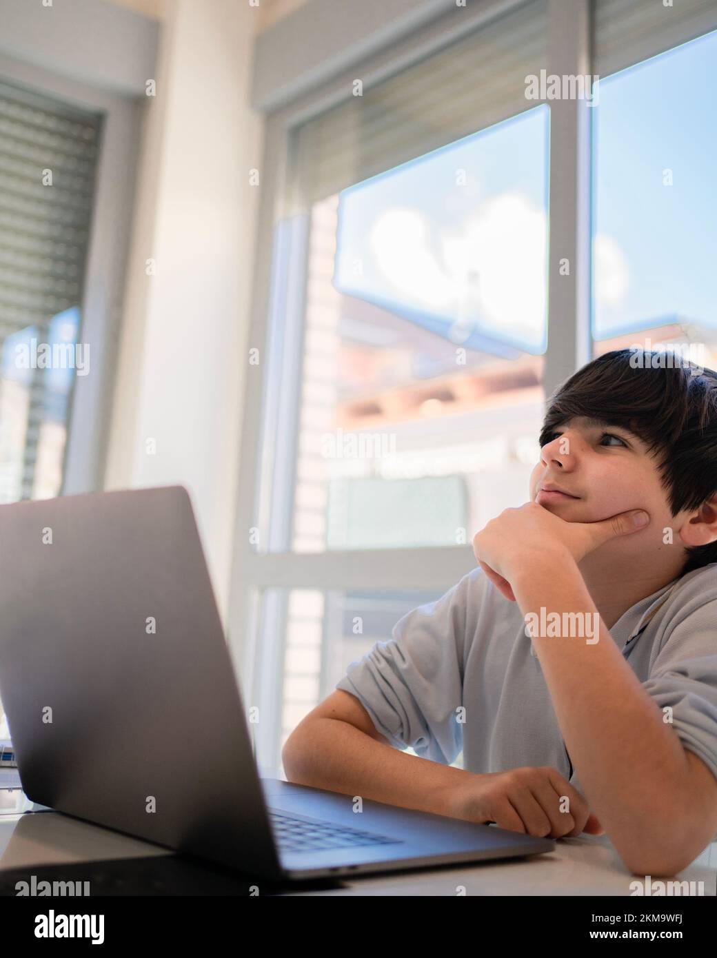 Kid sitting and thinking with laptop and table on window background at ...