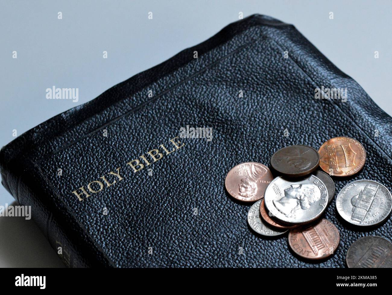 A closeup of the Holy Bible with coins on its black cover, isolated on ...
