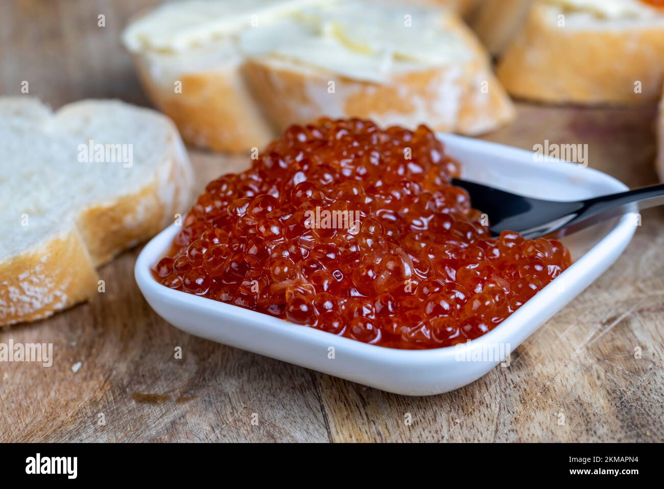red salmon or trout caviar with white baguette and butter, making ...