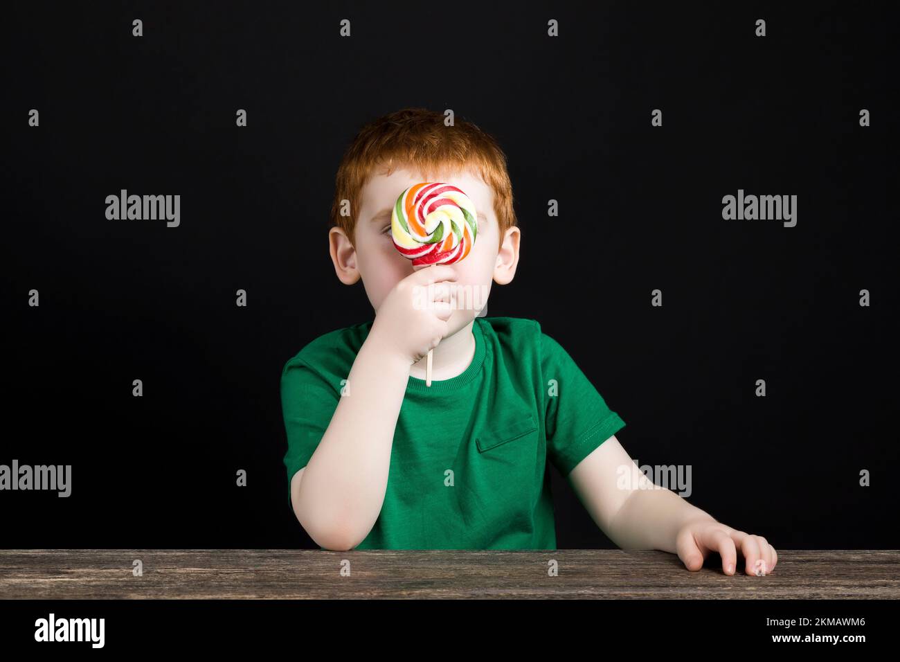 a red-haired boy with a beautiful face eats a sweet multi-colored candy ...