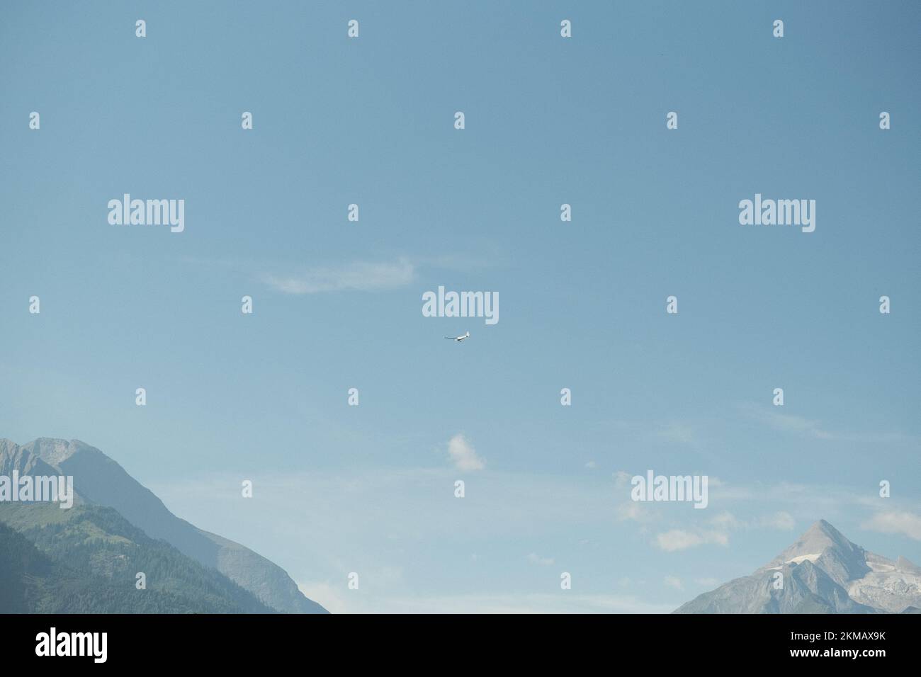 A plane flying high in the clear blue sky with mountains in the ...