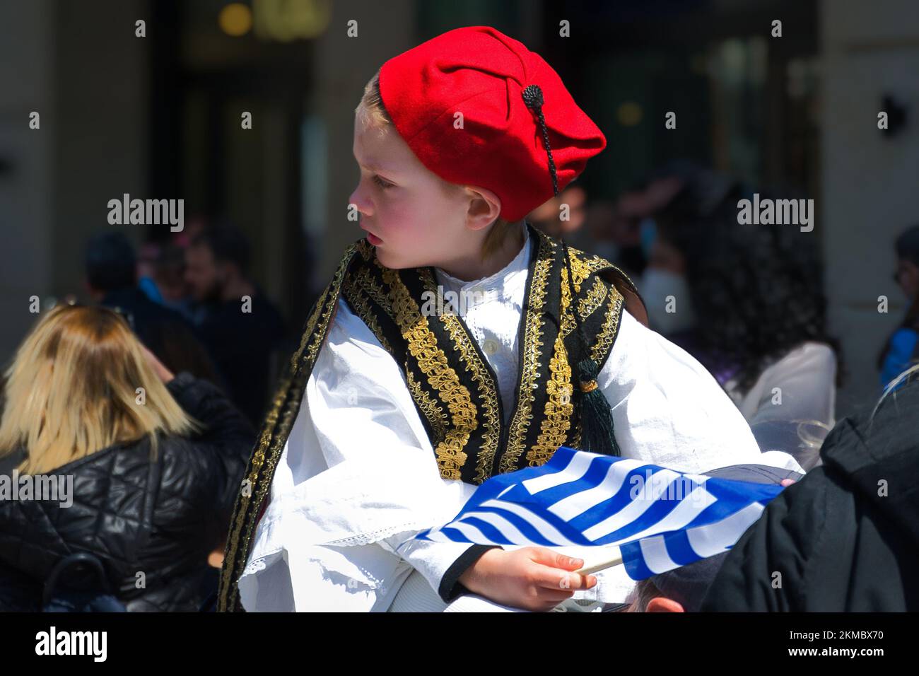 A young child in traditional Greek costume holds a flag on a national ...