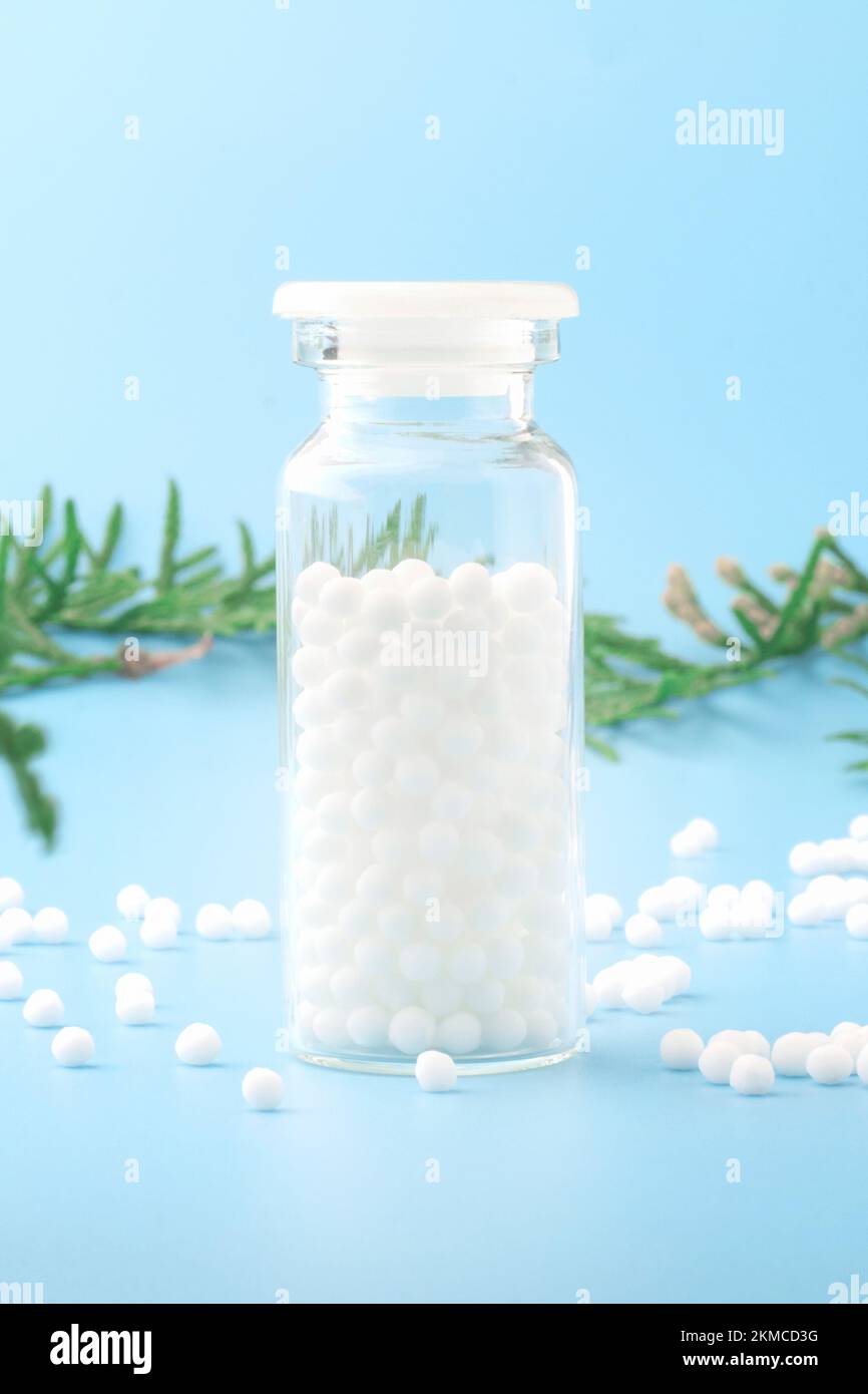 Homeopathic globules and glass bottle near with fresh juniper branches ...