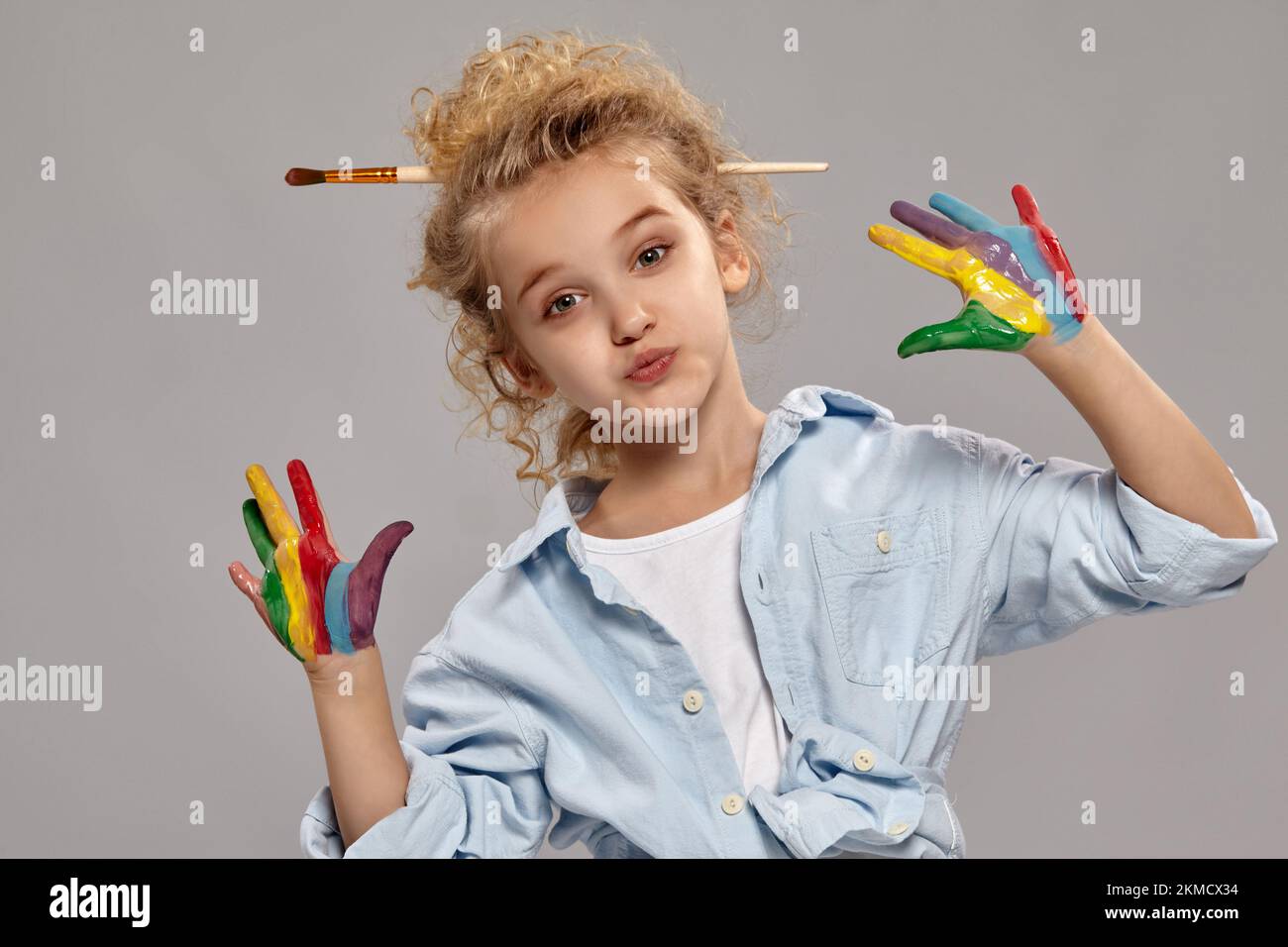 Beautiful little girl with a painted fingers is posing on a gray ...