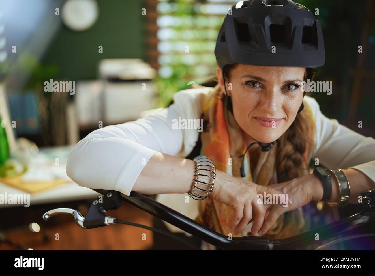 Portrait of stylish 40 years old business woman in bike helmet with bicycle in modern eco office ...