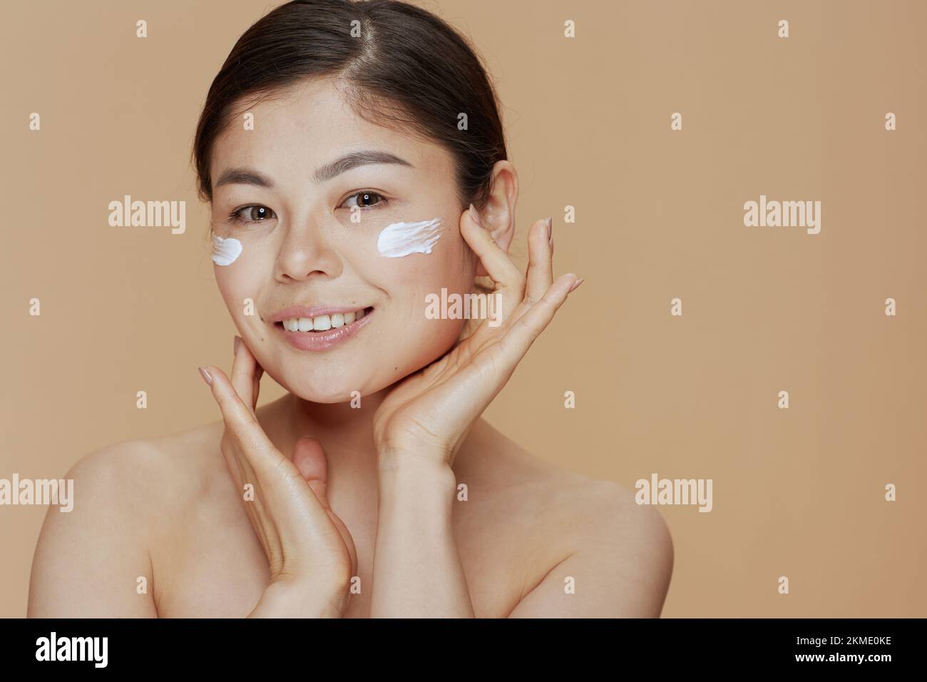 Portrait of modern asian woman with facial cream on face against beige ...