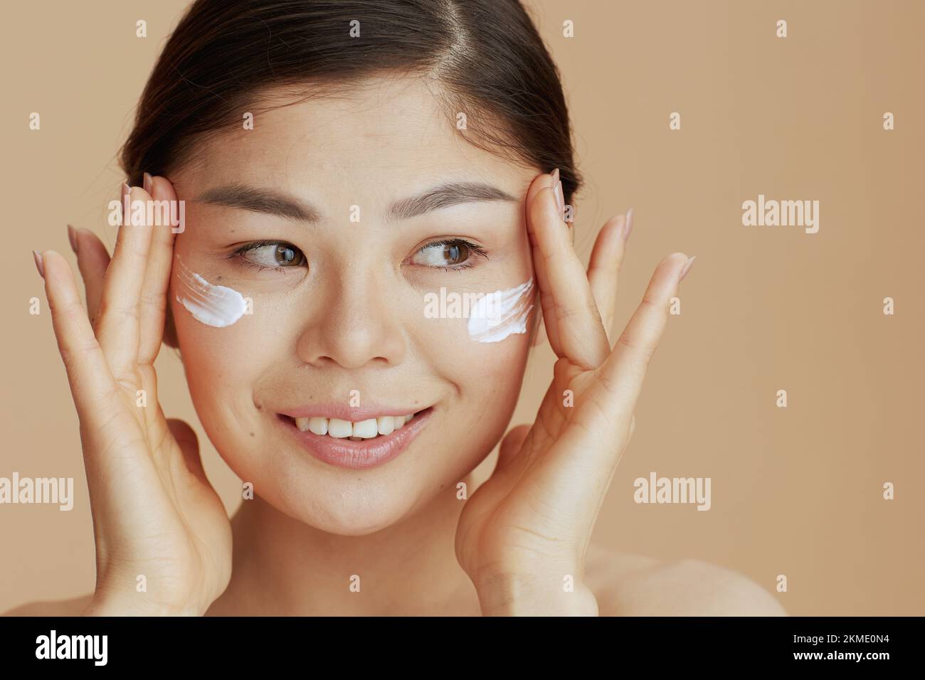 Portrait of modern asian female with facial cream on face on beige ...