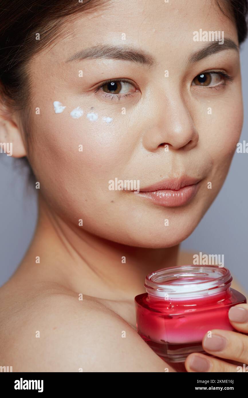 young woman with facial cream jar and eye cream on face against blue ...