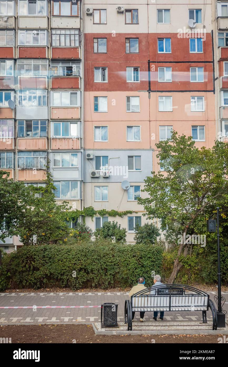 An old couple sitting on the bench while facing a tall apartment ...