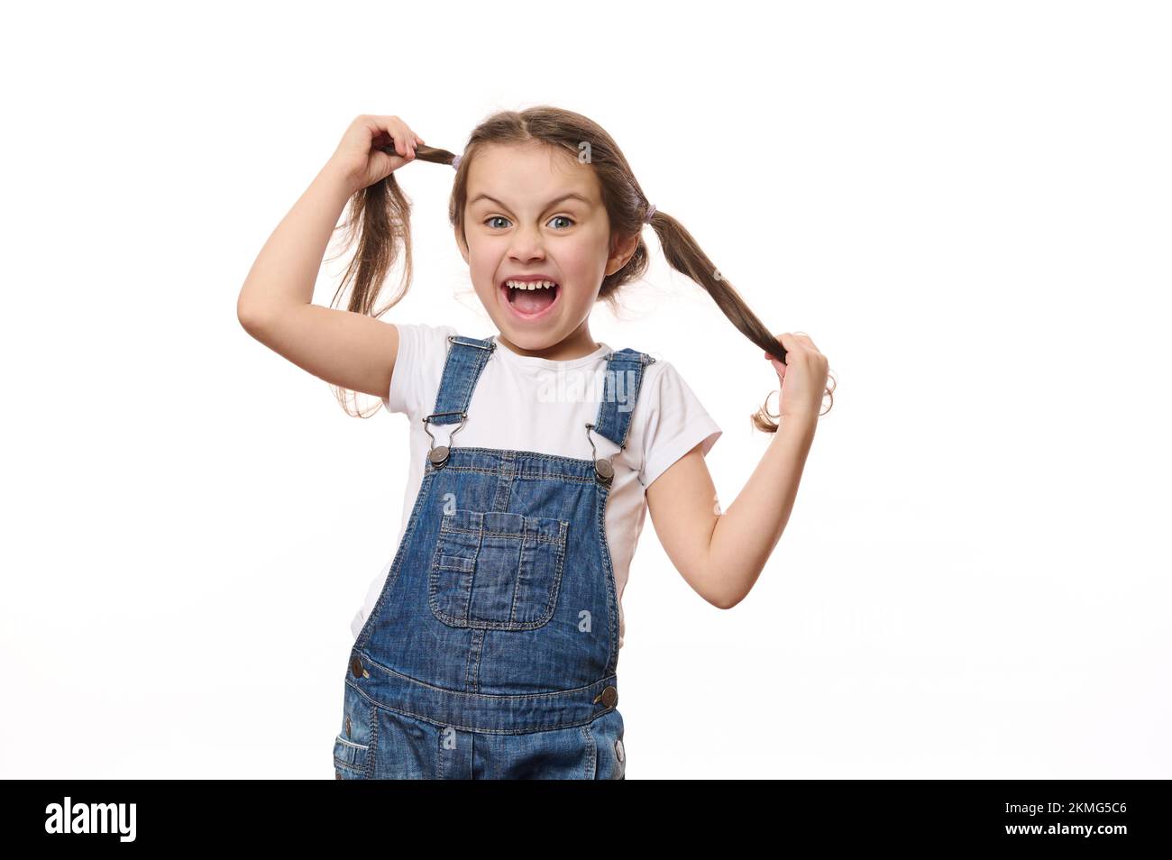 Mischievous little girl with two ponytails, in blue denim overalls ...