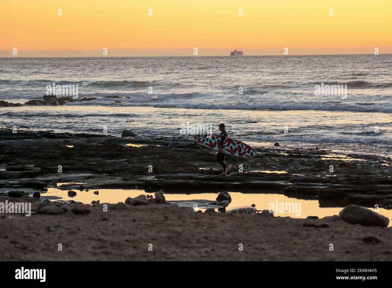 A Surfer walking on a rocky beach during sunset Stock Photo - Alamy