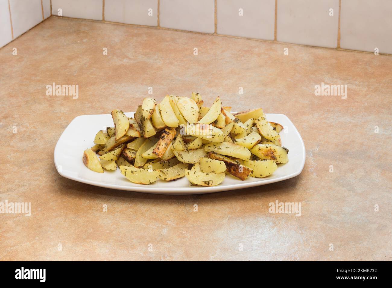 A large white ceramic platter filled with baked rosemary potatoes sits ...