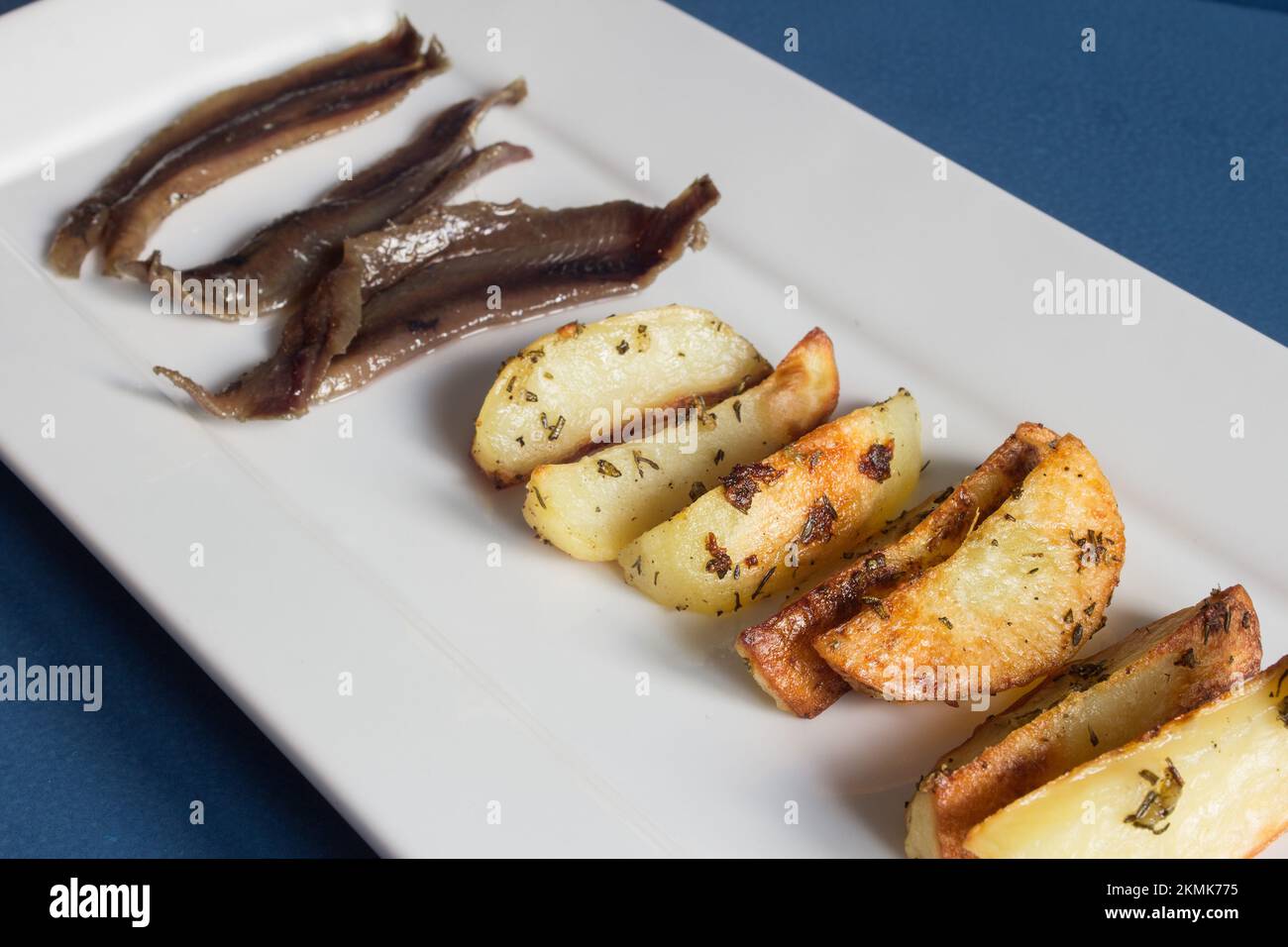 A rectangular white ceramic platter with baked rosemary potatoes in the ...