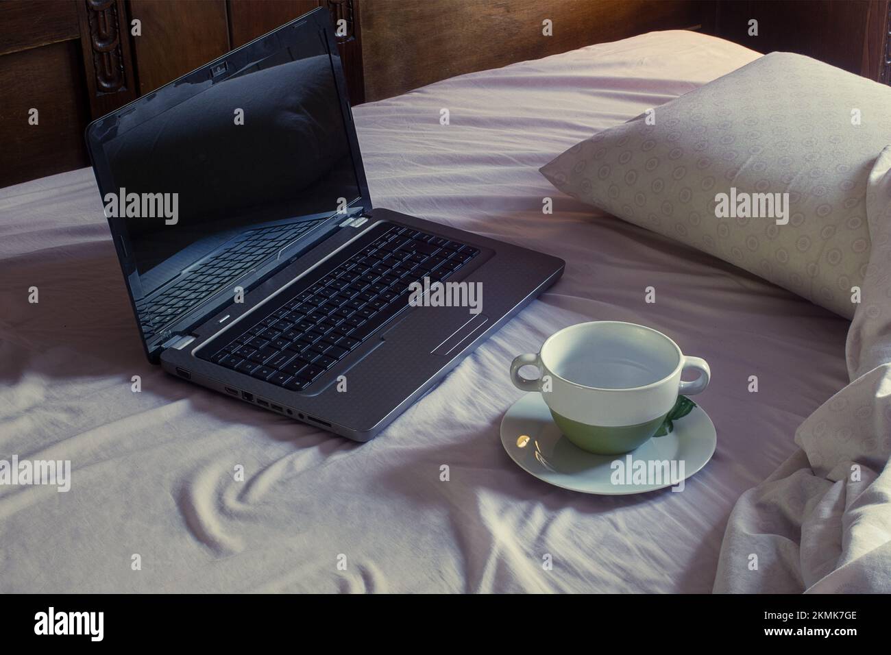 An empty mug on a dirty saucer next to an open laptop on an unmade ...