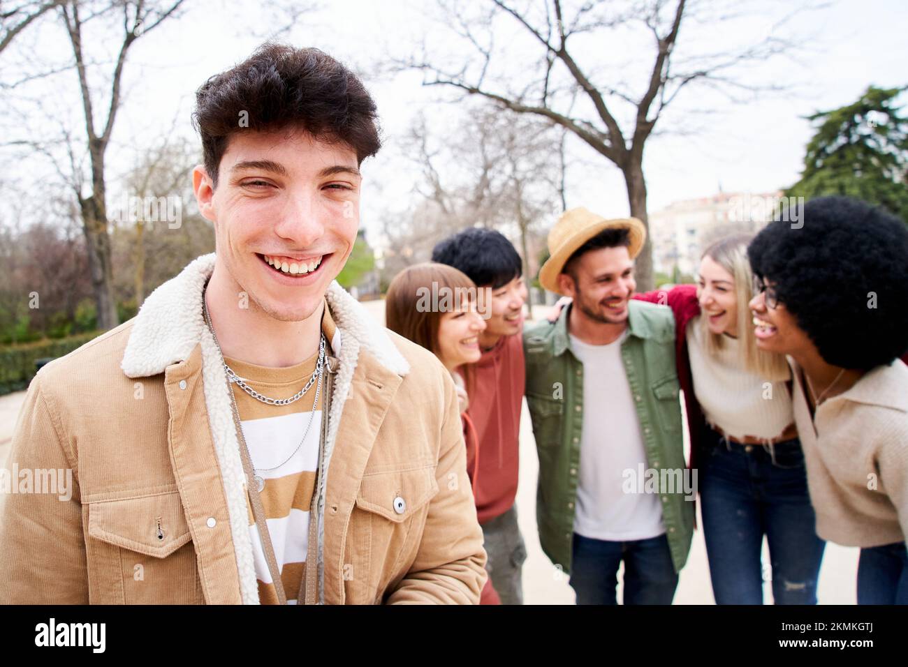 Young smiling guy looking at the camera outdoors with group of friends ...
