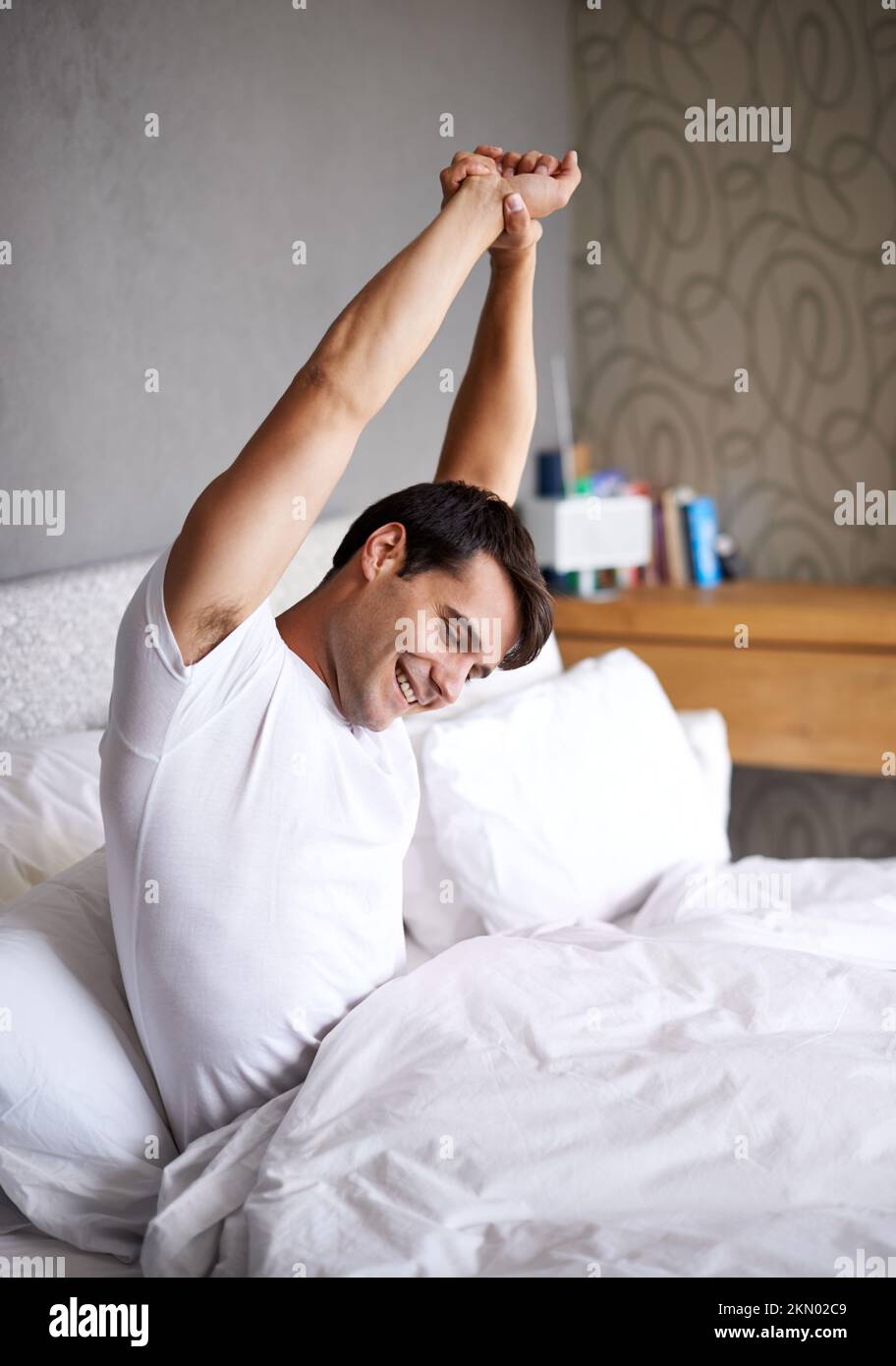 Getting in a good post-wake up stretch. a young man stretching in bed while waking up Stock ...