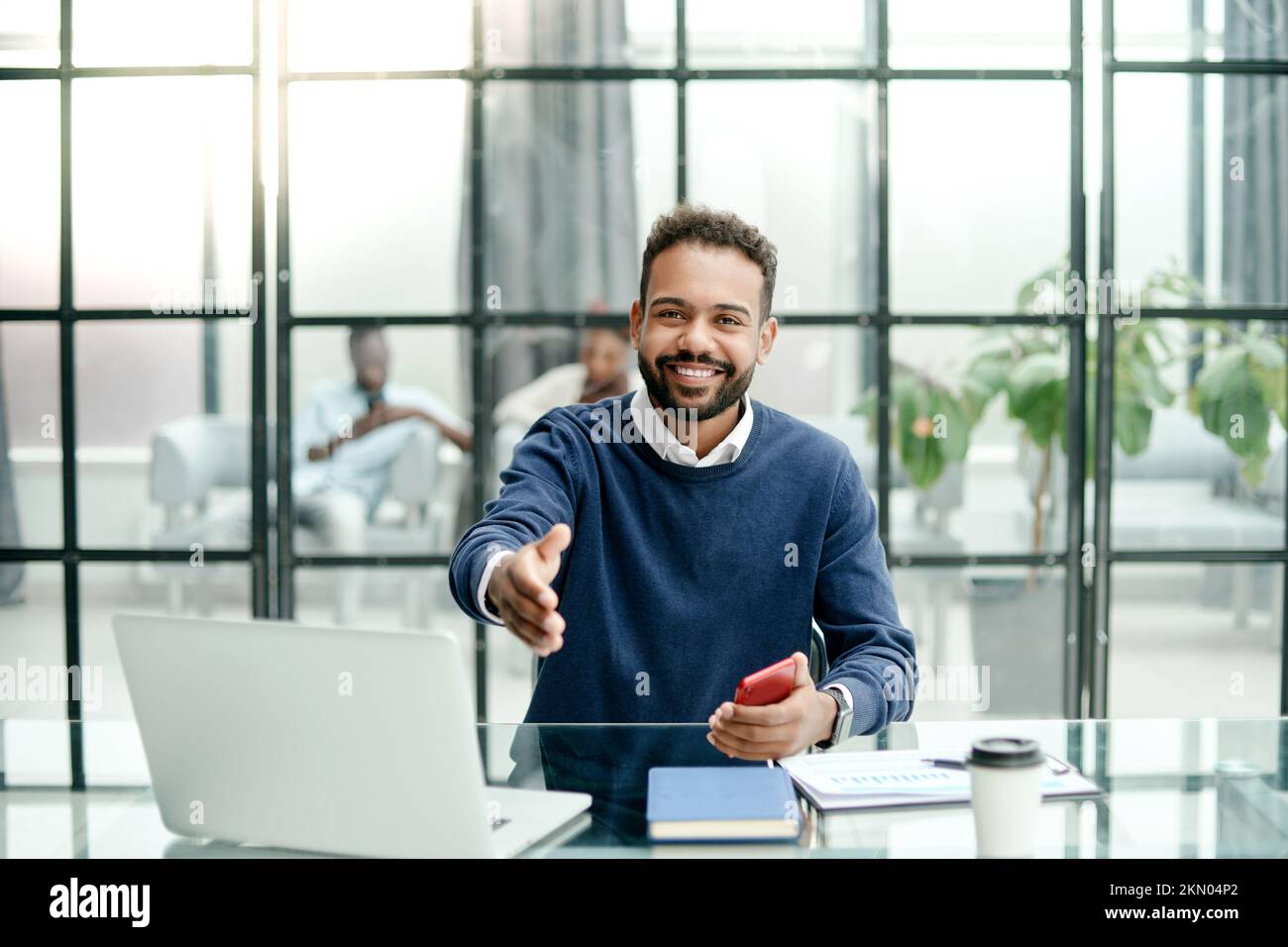 businessman reaching out for a handshake while sitting at his desk in ...