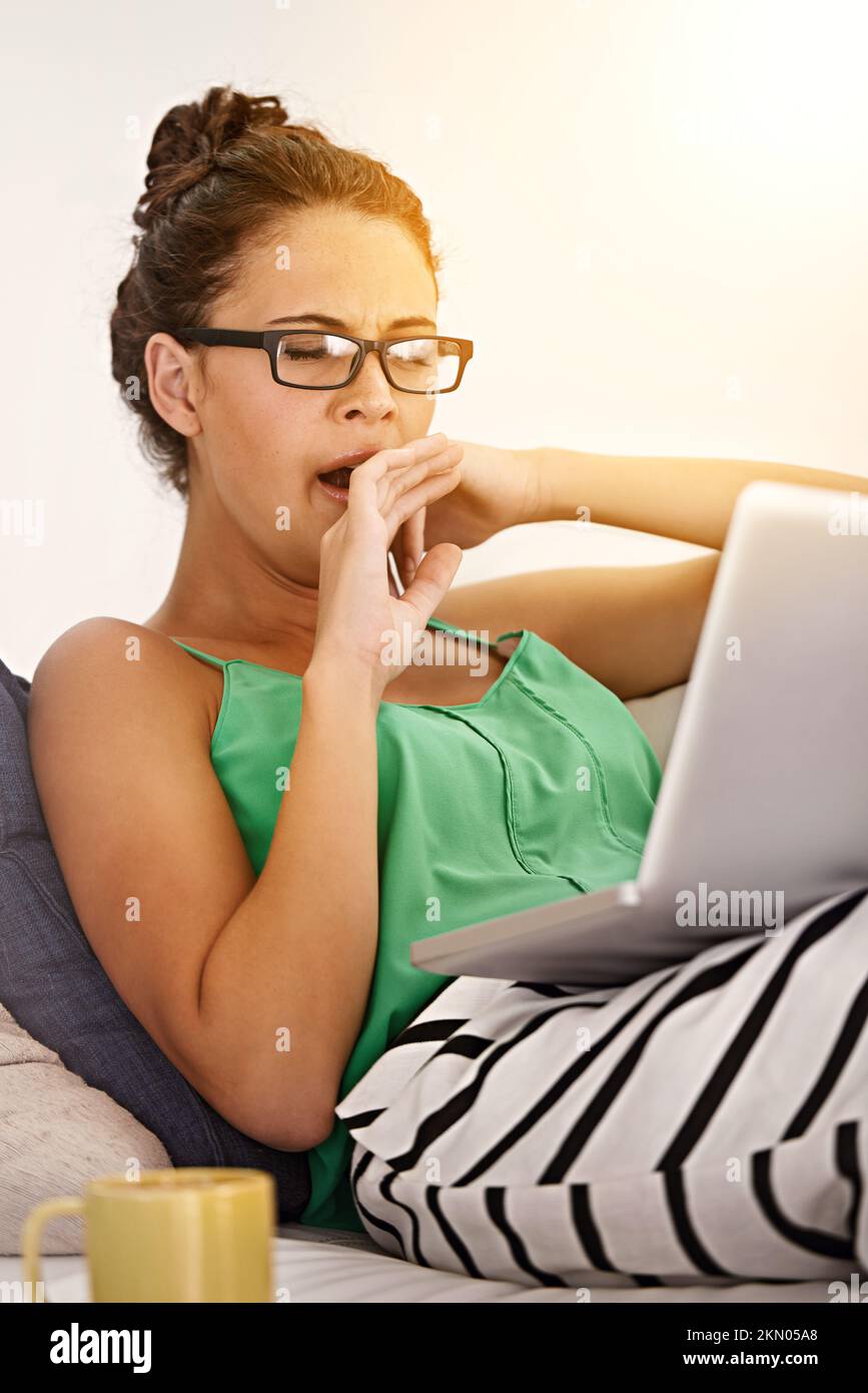 This is taking forever. a young woman yawning while using her laptop at ...