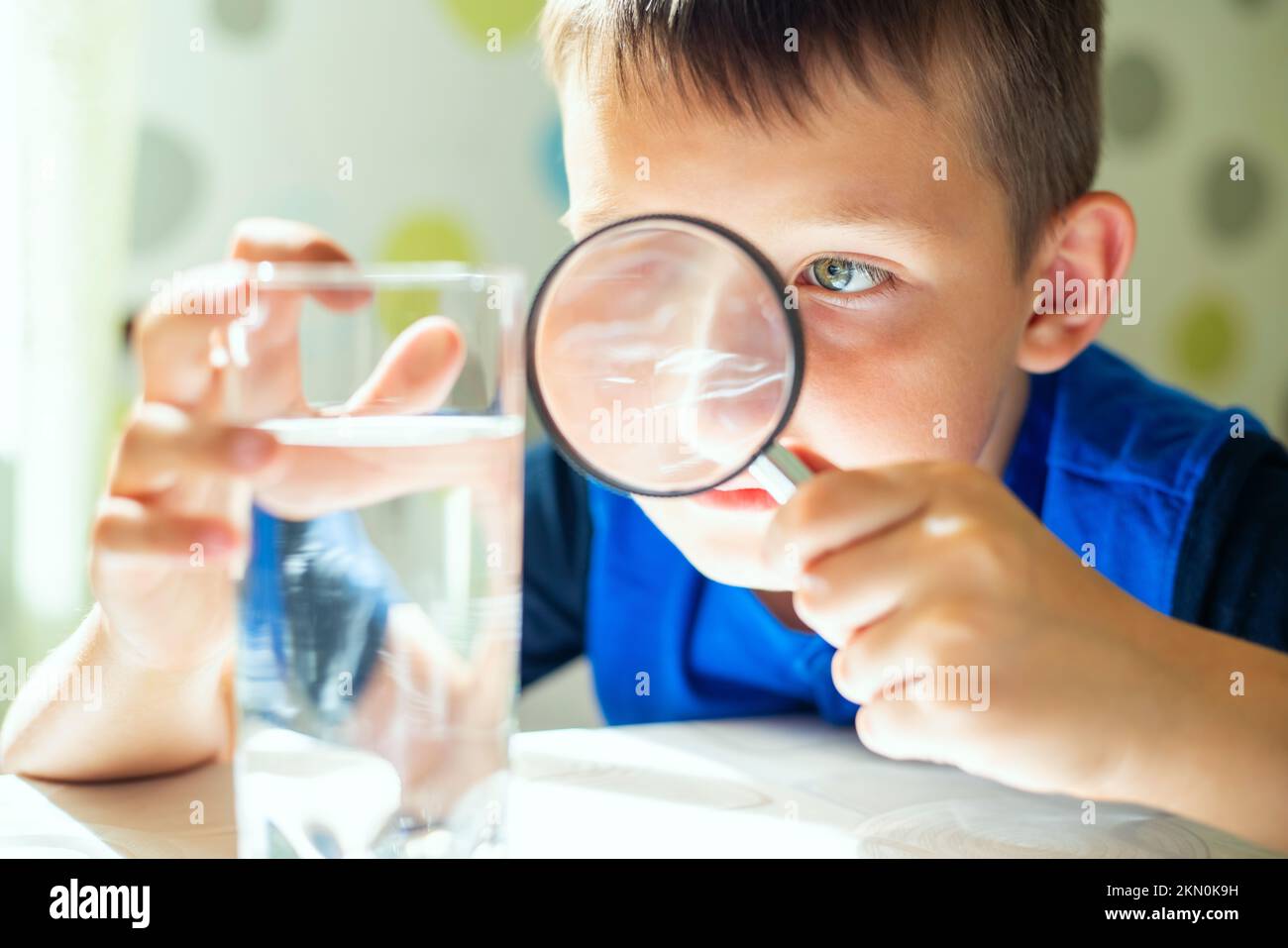 The child boy looking at water in a glass through magnifying glass ...