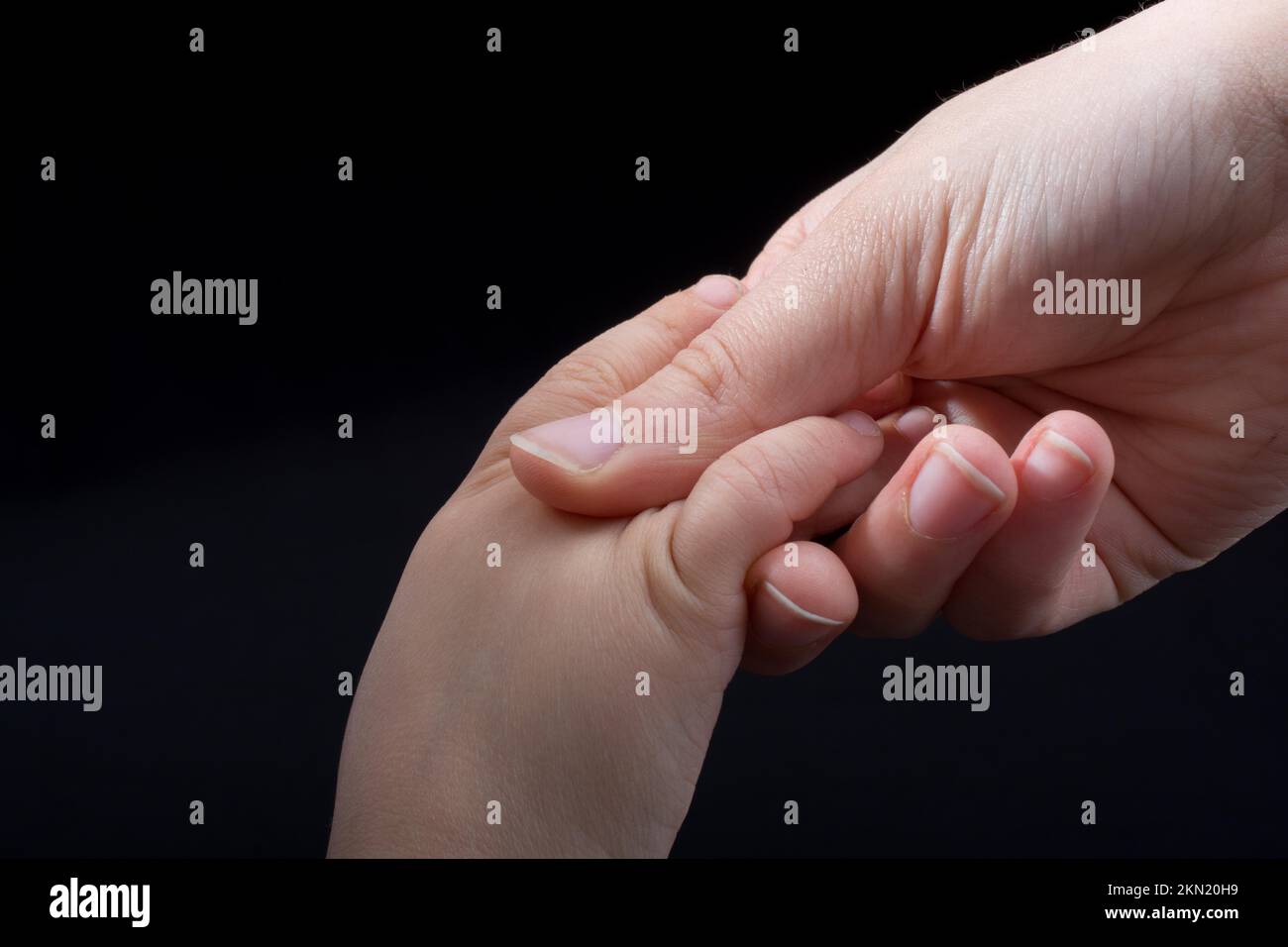Adult and child hold hands in black background Stock Photo - Alamy