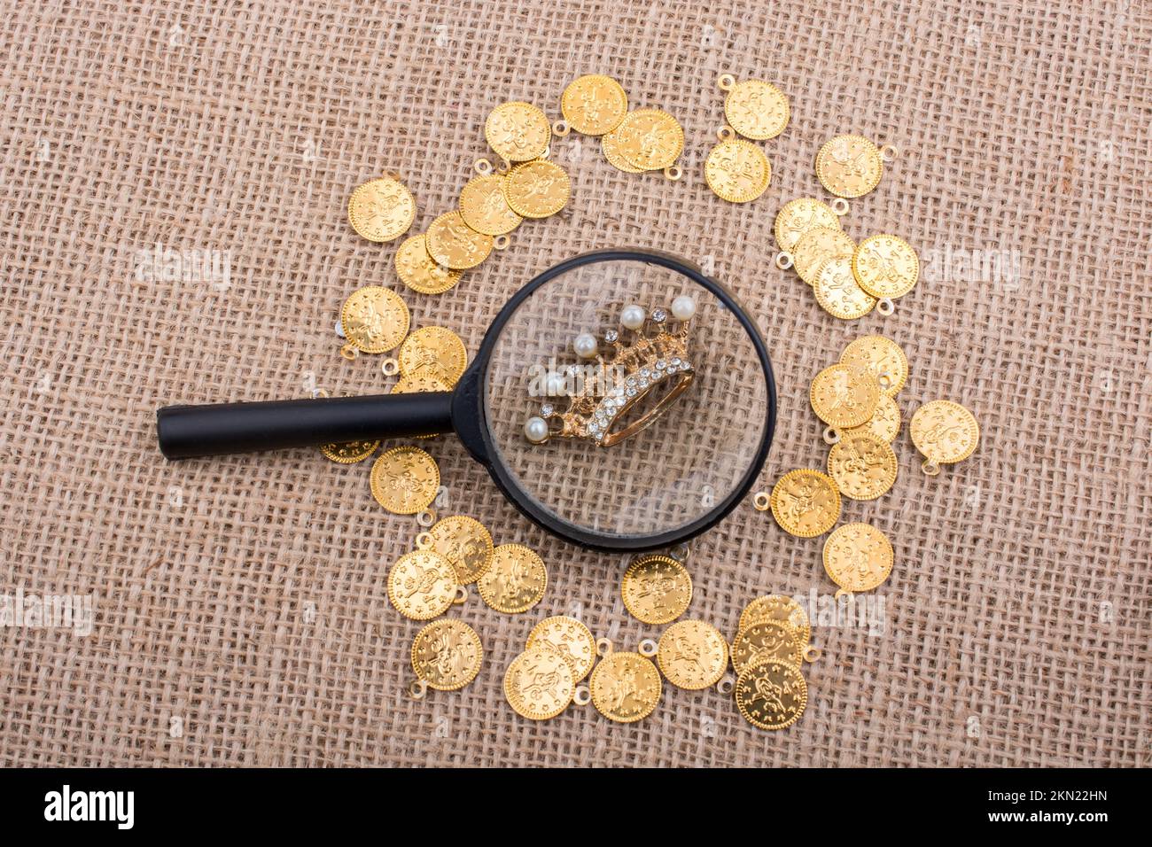 Crown under magnifying glass with fake gold coins Stock Photo - Alamy
