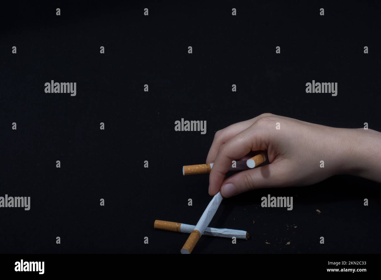 Hand is holding crossed cigarettes on black background Stock Photo - Alamy