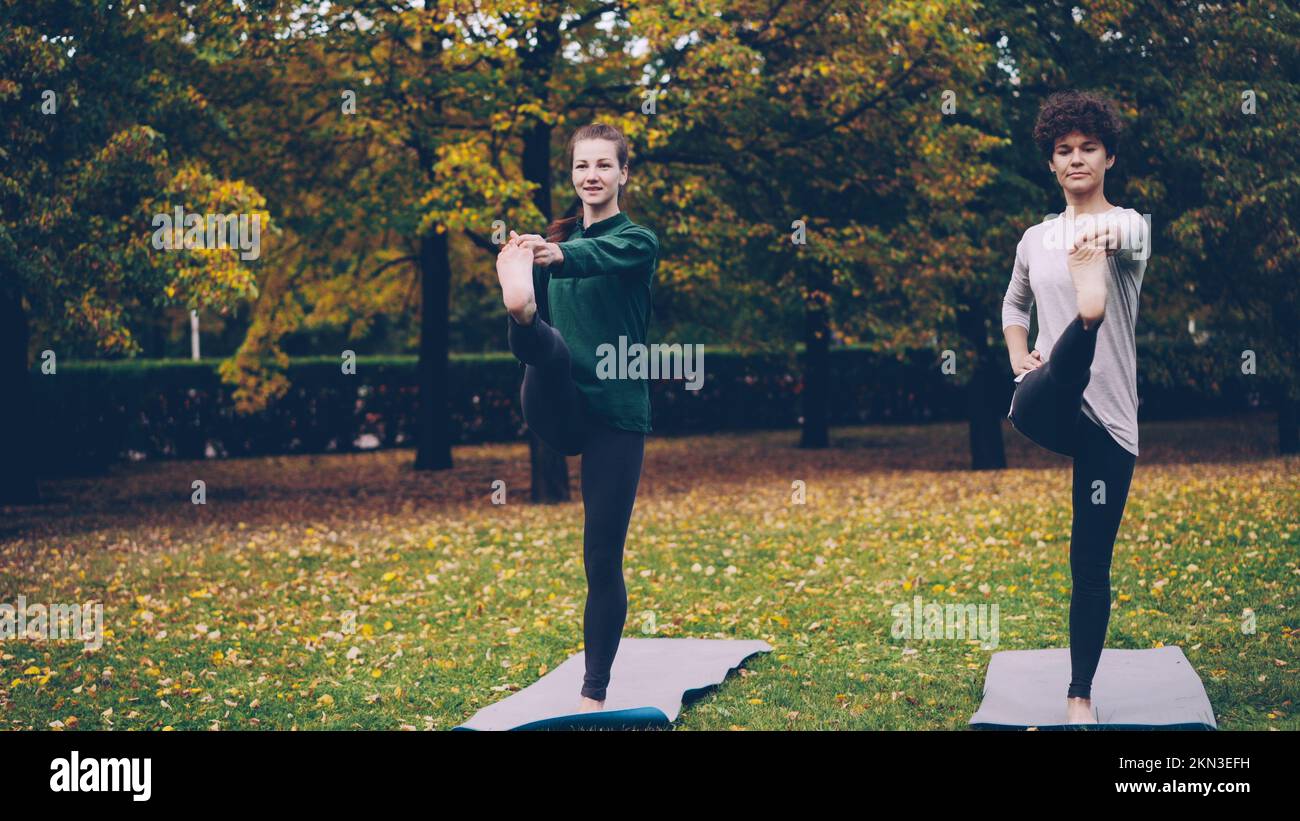 Couple of attractive girls are doing yoga in park practising balancing ...